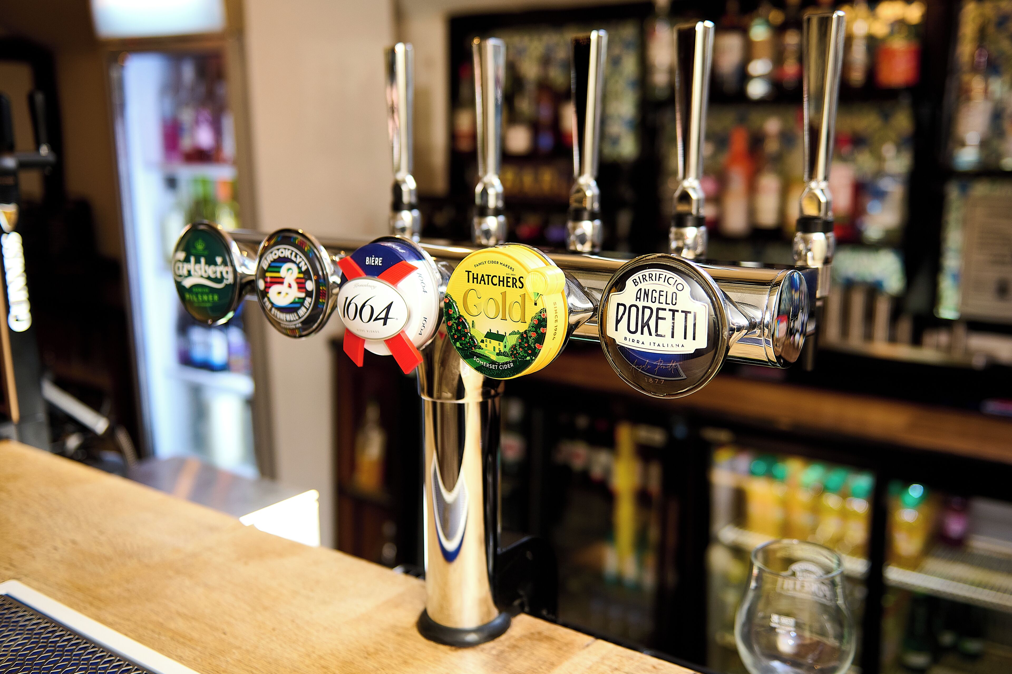 Uma torneira com várias etiquetas de cerveja, incluindo marcas como Carlsberg e Brooklyn.