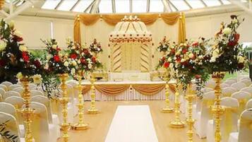 Decoração de casamento com um corredor branco, candelabros dourados e arranjos florais.