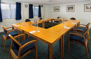 Uma sala de conferências com uma mesa comprida, cadeiras e um relógio na parede.