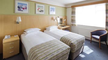 Quarto de hotel com duas camas, uma escrivaninha, uma cadeira e uma janela com cortinas.