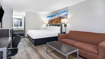 Quarto de hotel com uma cama, um sofá marrom, uma mesinha, uma escrivaninha com cadeira e um quadro na parede.