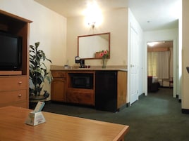 Quarto de hotel com secretária de madeira, televisão, micro-ondas, pia e espelho.