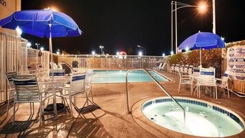 Uma área de piscina com espreguiçadeiras, guarda-sóis e uma banheira de hidromassagem.