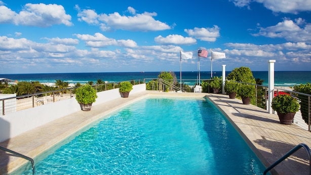 Área da piscina com vista para o oceano, bandeiras dos Estados Unidos e Bentley, e plantas em vasos.