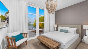 Quarto moderno com uma cama grande, um banquinho de madeira, um candelabro e vista para o exterior.