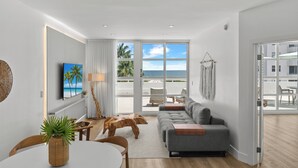 Sala de estar moderna com sofá, mesa de jantar e vista para a praia.