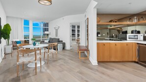 Uma sala de estar moderna com área de jantar, cozinha e janelas amplas com vista para o oceano.
