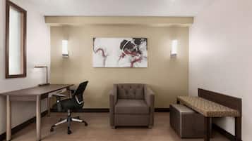 Quarto de hotel com escrivaninha, cadeira de escritório, sofá, banqueta e um quadro na parede.