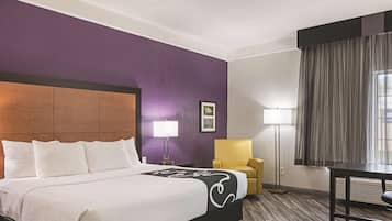 Quarto de hotel com uma cama grande, uma poltrona amarela, uma escrivaninha e uma janela com cortinas.