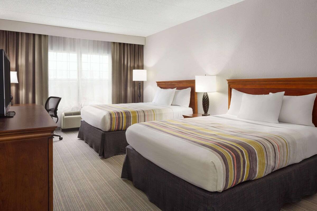 Quarto de hotel com duas camas, uma escrivaninha, uma cadeira e uma televisão.