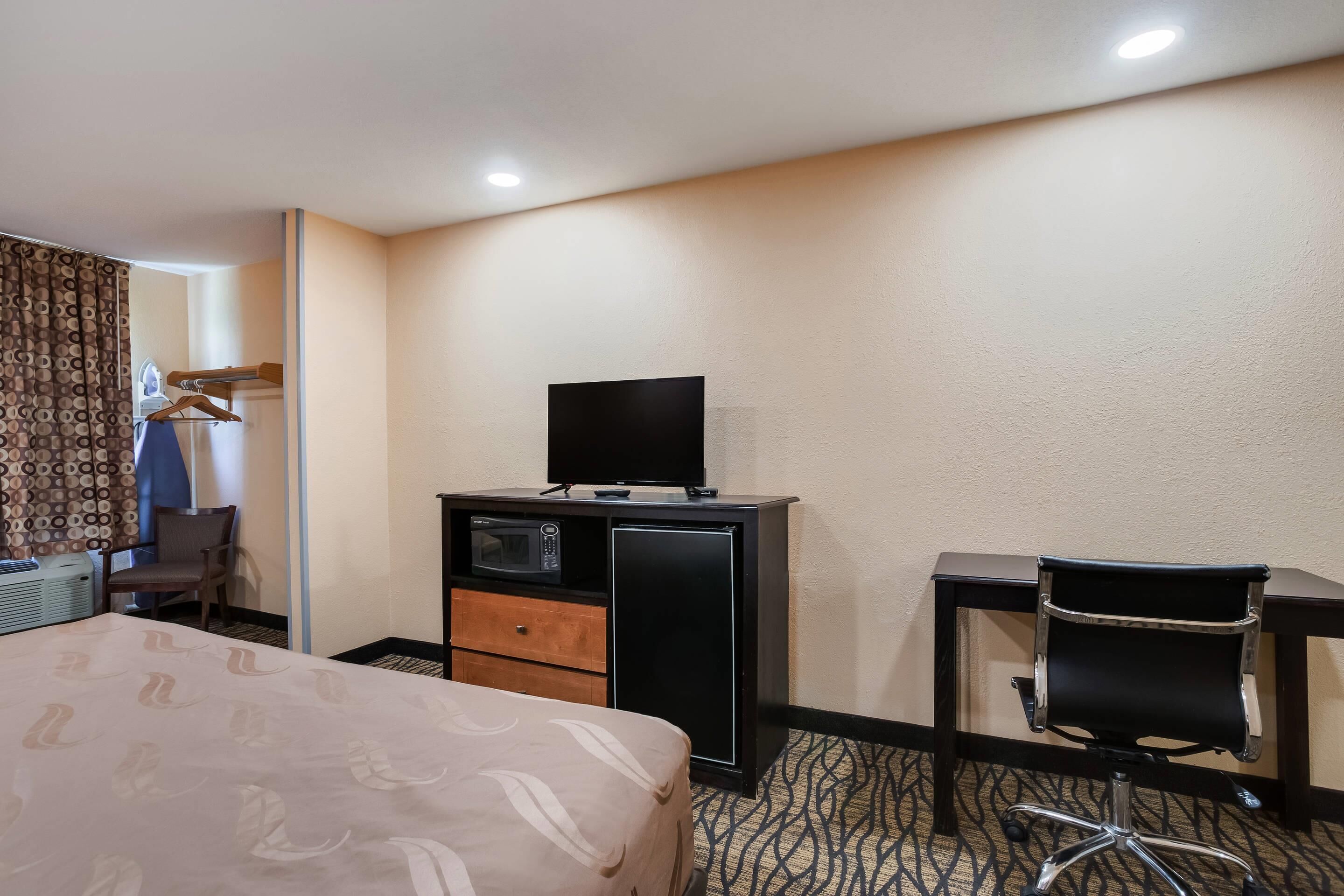 Quarto de hotel com cama, escrivaninha com cadeira, televisão e guarda-roupa.
