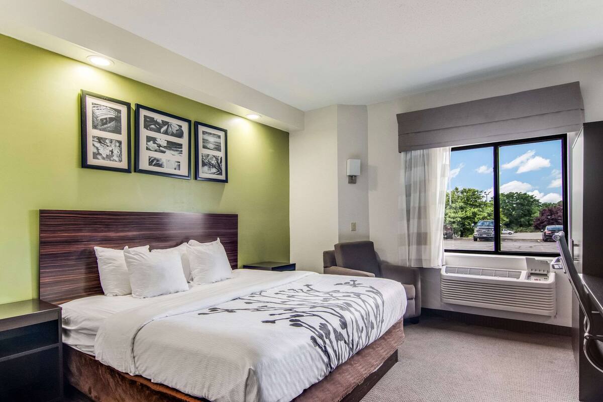 Quarto de hotel com uma cama grande, uma escrivaninha, uma cadeira e janela com vista para o exterior.
