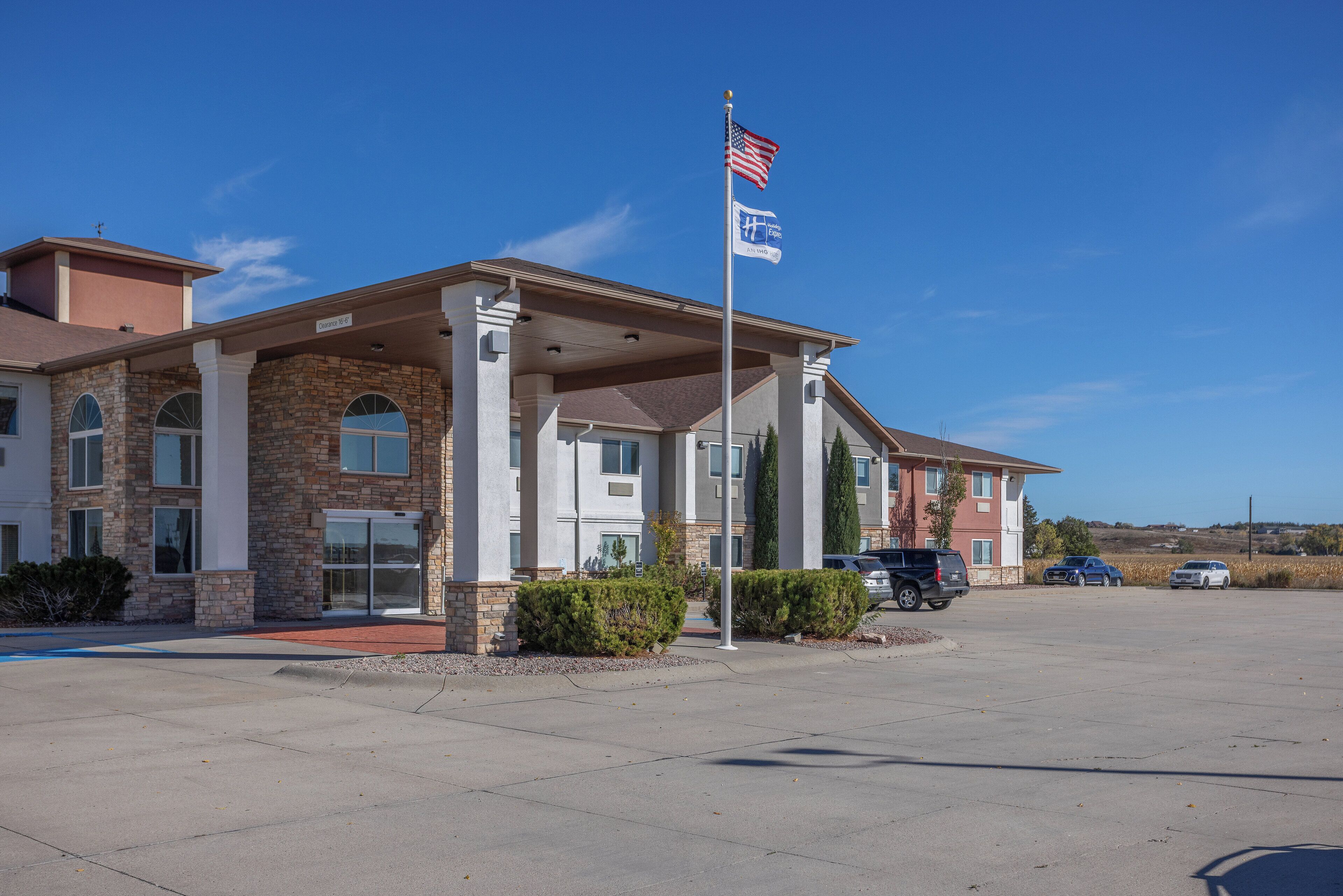 Hotel com entrada coberta, mastro com a bandeira americana e estacionamento com vários carros.