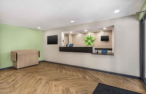 Uma área de recepção com uma mesa de madeira, uma parede verde e um piso em padrão herringbone.