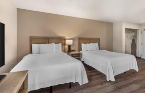 Quarto de hotel com duas camas, uma mesa de cabeceira, um abajur e um guarda-roupa.
