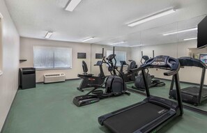 Centro de fitness com esteiras, elípticos e um espelho grande.