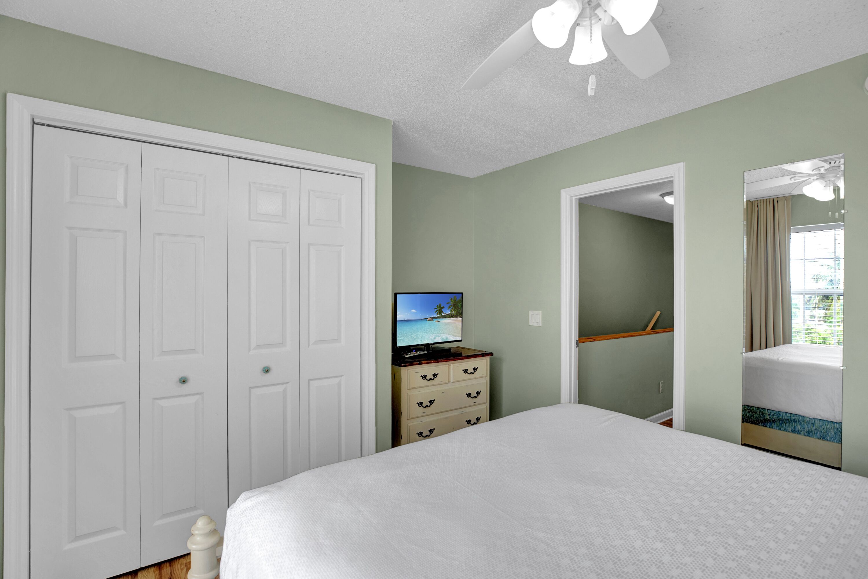 Quarto com cama, cômoda, televisão e ventilador de teto.