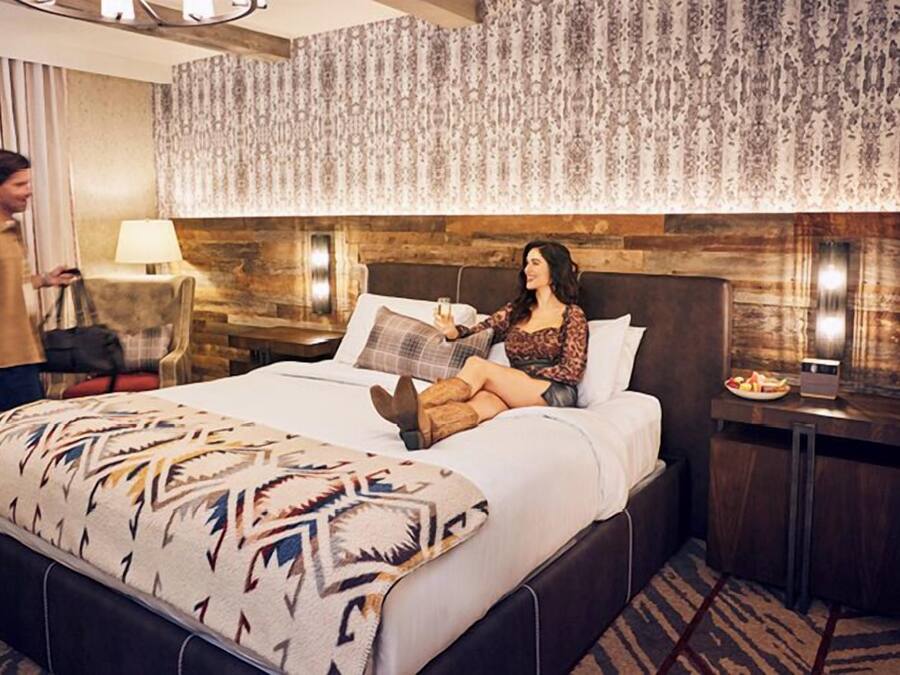 Quarto de hotel com uma cama grande, mesa de cabeceira, abajur e cabeceira estampada.