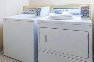 Duas máquinas de lavar roupa frontais brancas, com painel de controlo e uma caixa de detergente Purex em cima.