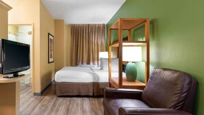 Quarto de hotel com cama, televisão, escrivaninha, cadeira e parede verde.