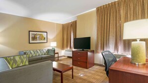 Quarto de hotel com sofá, televisão, escrivaninha e luminária.