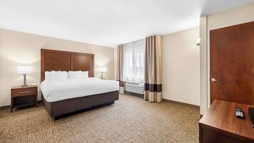 Quarto de hotel com uma cama grande, uma mesinha de cabeceira com abajur, uma escrivaninha com controle remoto e uma porta.