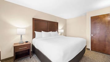 Quarto de hotel com uma cama grande, duas mesas de cabeceira com abajures, uma porta de madeira e piso coberto por carpete.