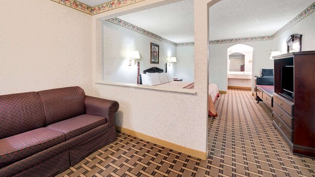 Quarto de hotel com carpete estampado, um sofá, uma televisão e um espelho refletindo o ambiente.