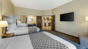 Quarto de hotel com uma cama grande, uma mesa, uma cadeira, uma televisão e um banheiro visível através de uma porta aberta.