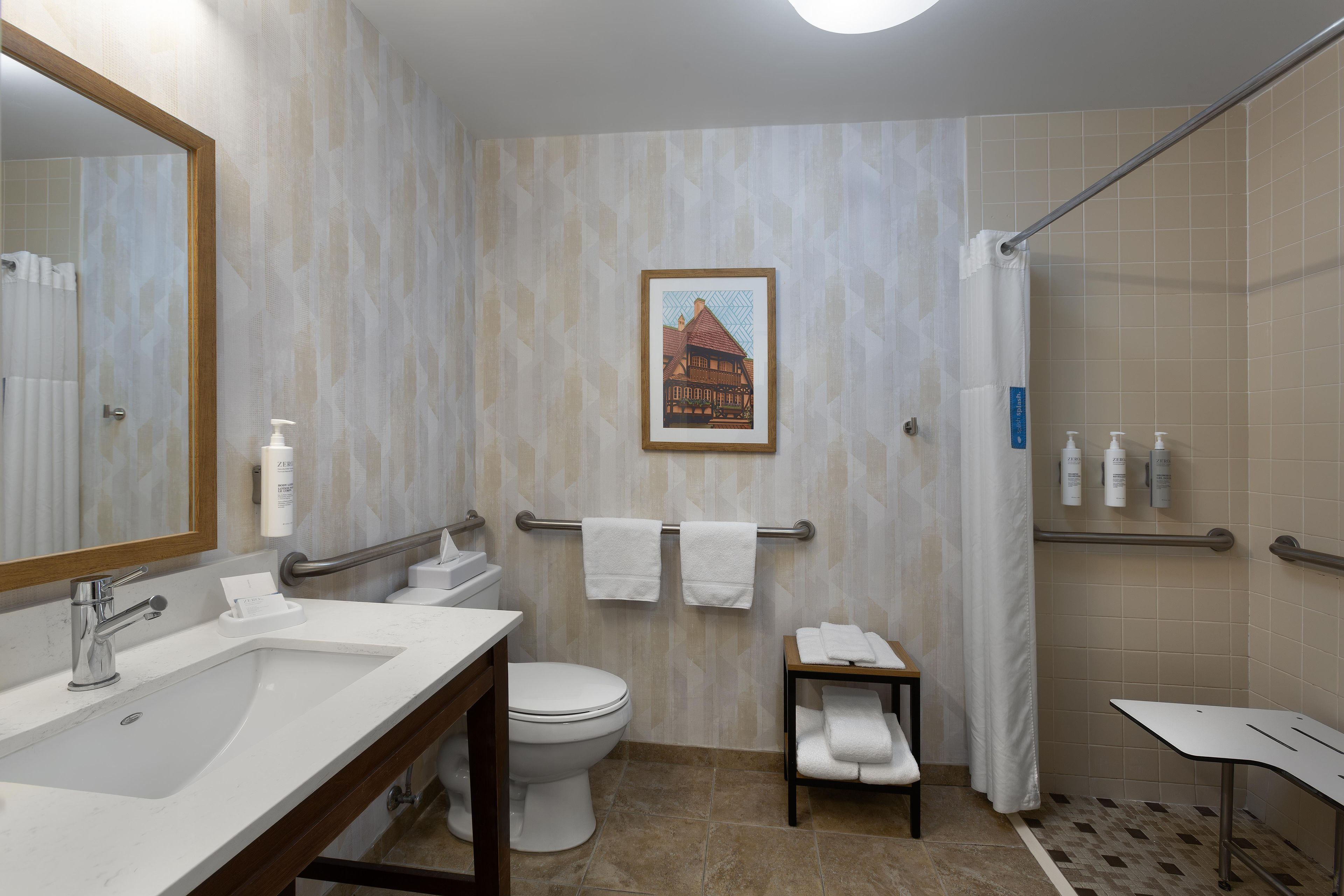 Casa de banho com lavatório, sanita e chuveiro, e um quadro na parede.