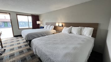 Quarto de hotel com duas camas, uma janela grande, uma escrivaninha e um abajur.