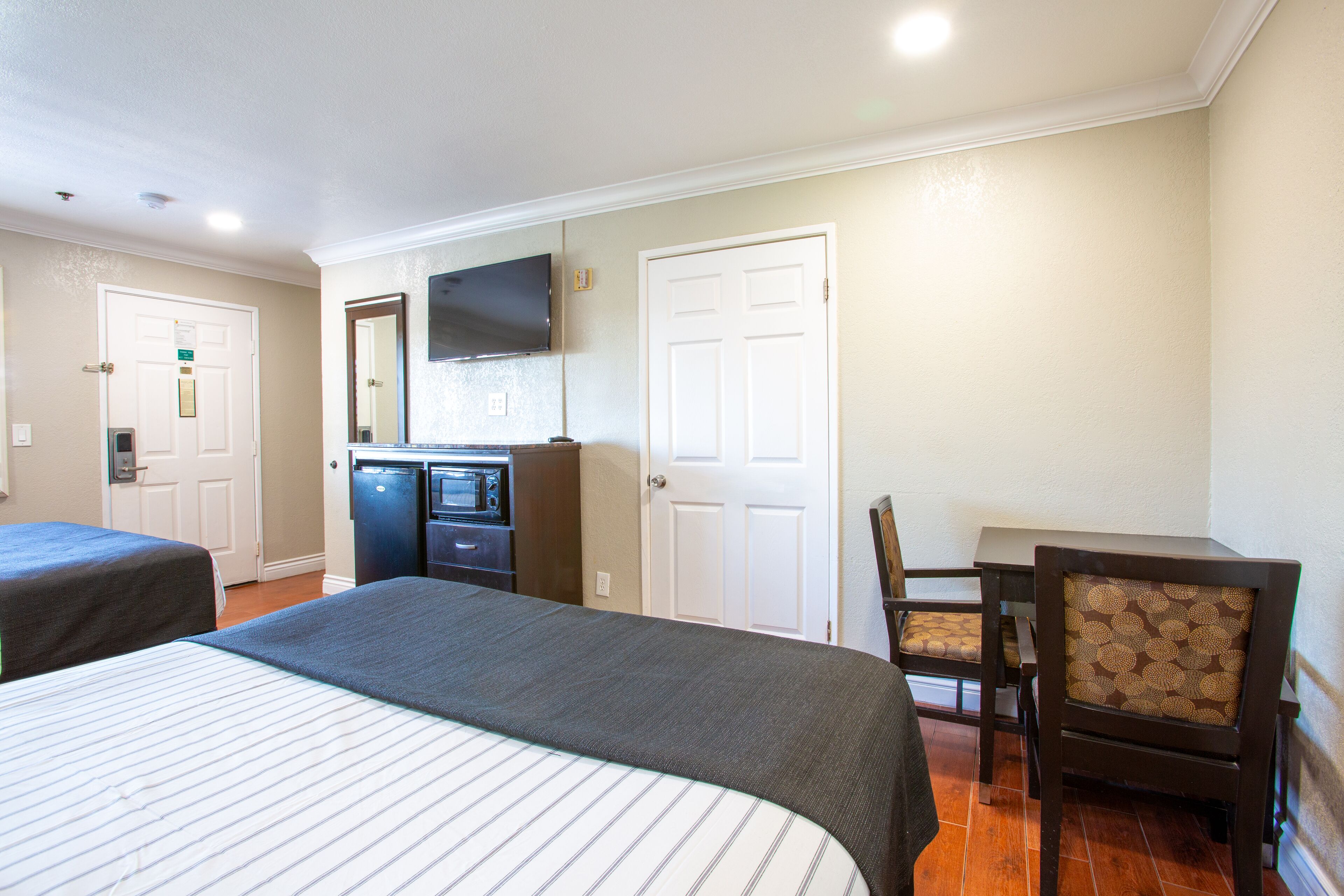 Quarto de hotel com duas camas, uma escrivaninha, uma cadeira, uma televisão e uma porta.