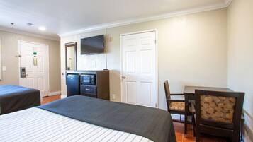 Quarto de hotel com duas camas, uma escrivaninha, uma cadeira, uma televisão e uma porta.