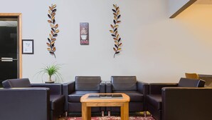 Um lobby moderno com um sofá de couro escuro, uma mesa de centro de madeira e obras de arte decorativas na parede.