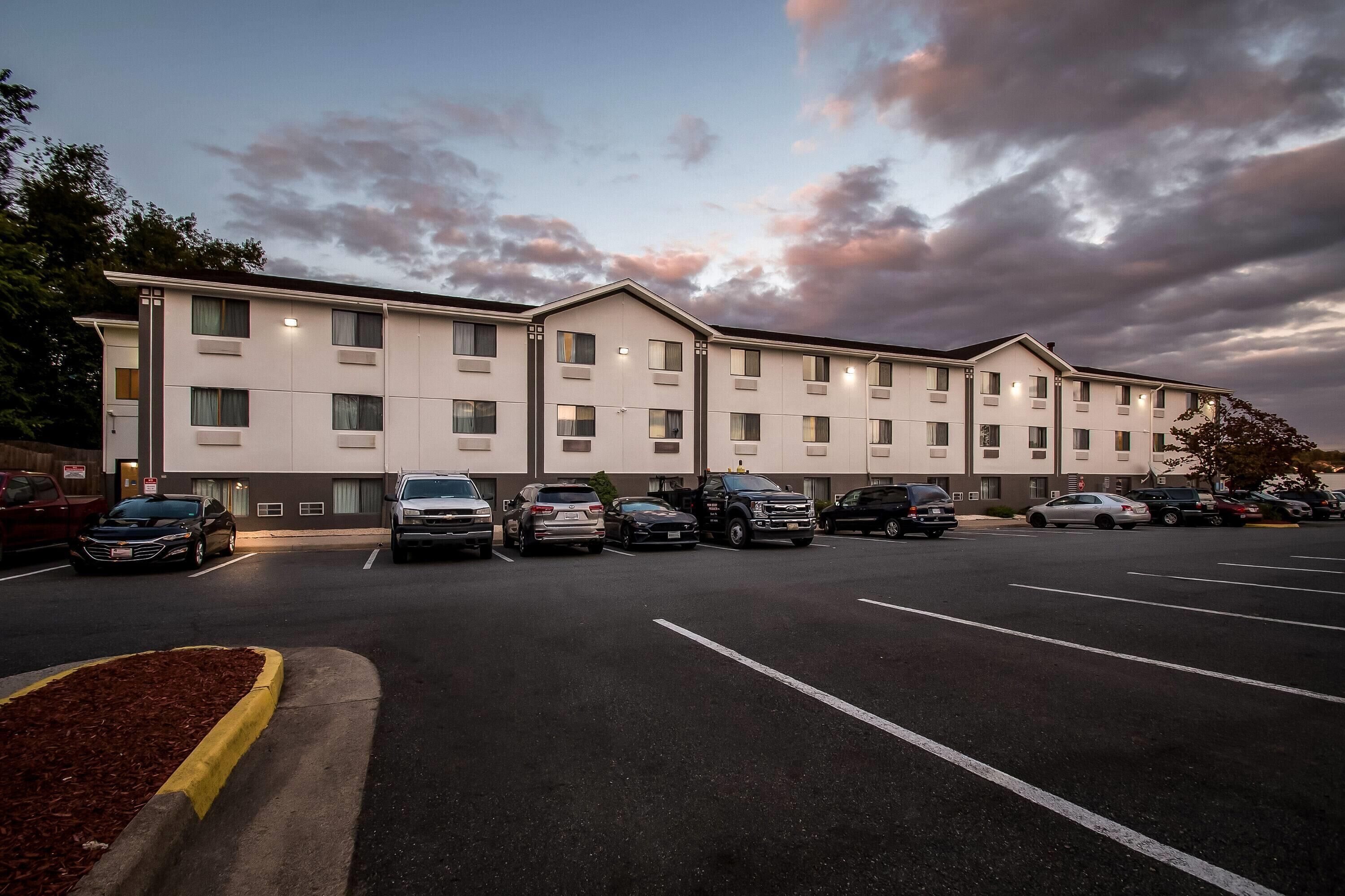 Um hotel com vários andares e uma fileira de vagas de estacionamento na frente.