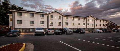 Um hotel com vários andares e uma fileira de vagas de estacionamento na frente.