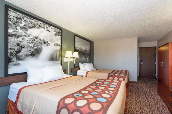 Quarto de hotel com duas camas, uma grande pintura emoldurada de uma cascata, uma mesa de cabeceira com abajur e um guarda-roupa.