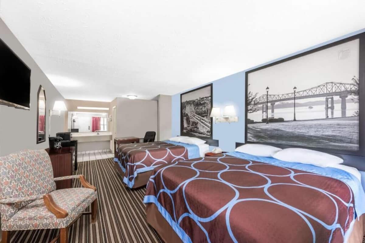 Quarto de hotel com duas camas, uma escrivaninha, uma cadeira e uma televisão.