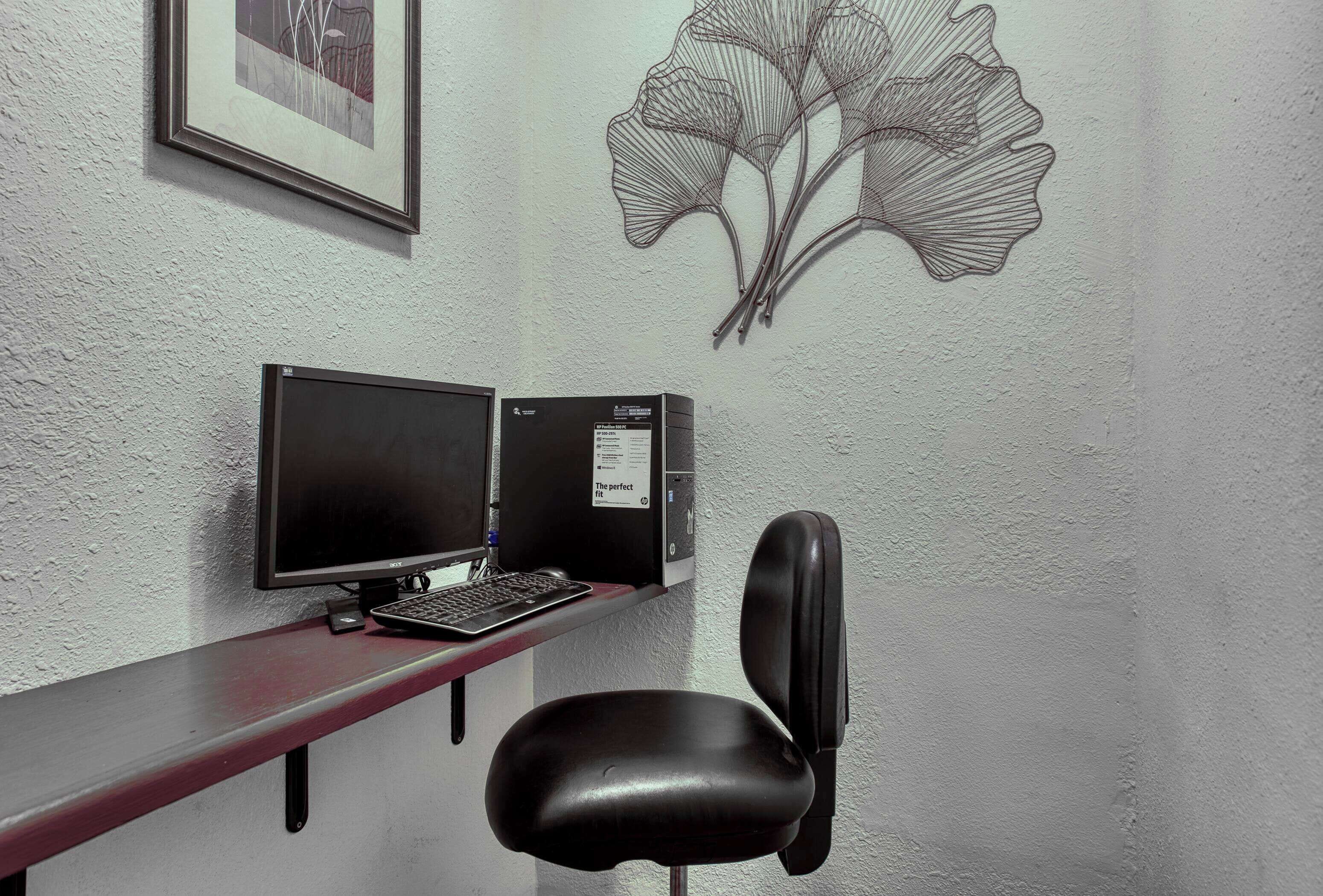 Uma escrivaninha com um computador, uma cadeira e um objeto decorativo na parede.