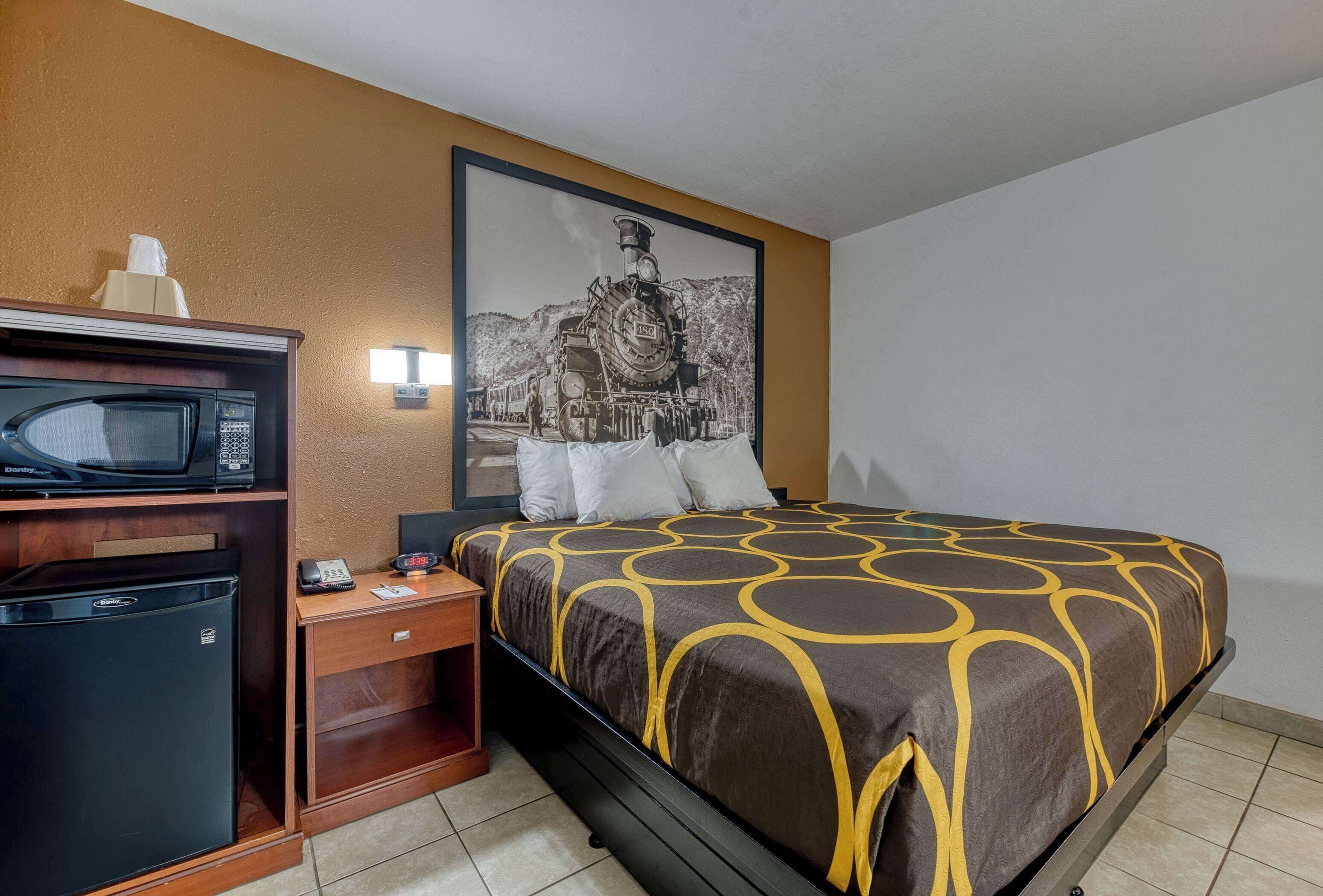 Quarto de hotel com cama, micro-ondas, frigorífico, mesa de cabeceira e um quadro na parede.