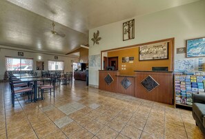 Um hall amplo com uma mesa de recepção, uma grande área de jantar com mesas e cadeiras, e piso em azulejos.