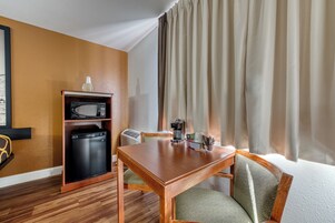 Quarto de hotel compacto com mesa de jantar de madeira, frigorífico embutido, micro-ondas e uma pequena cozinha.