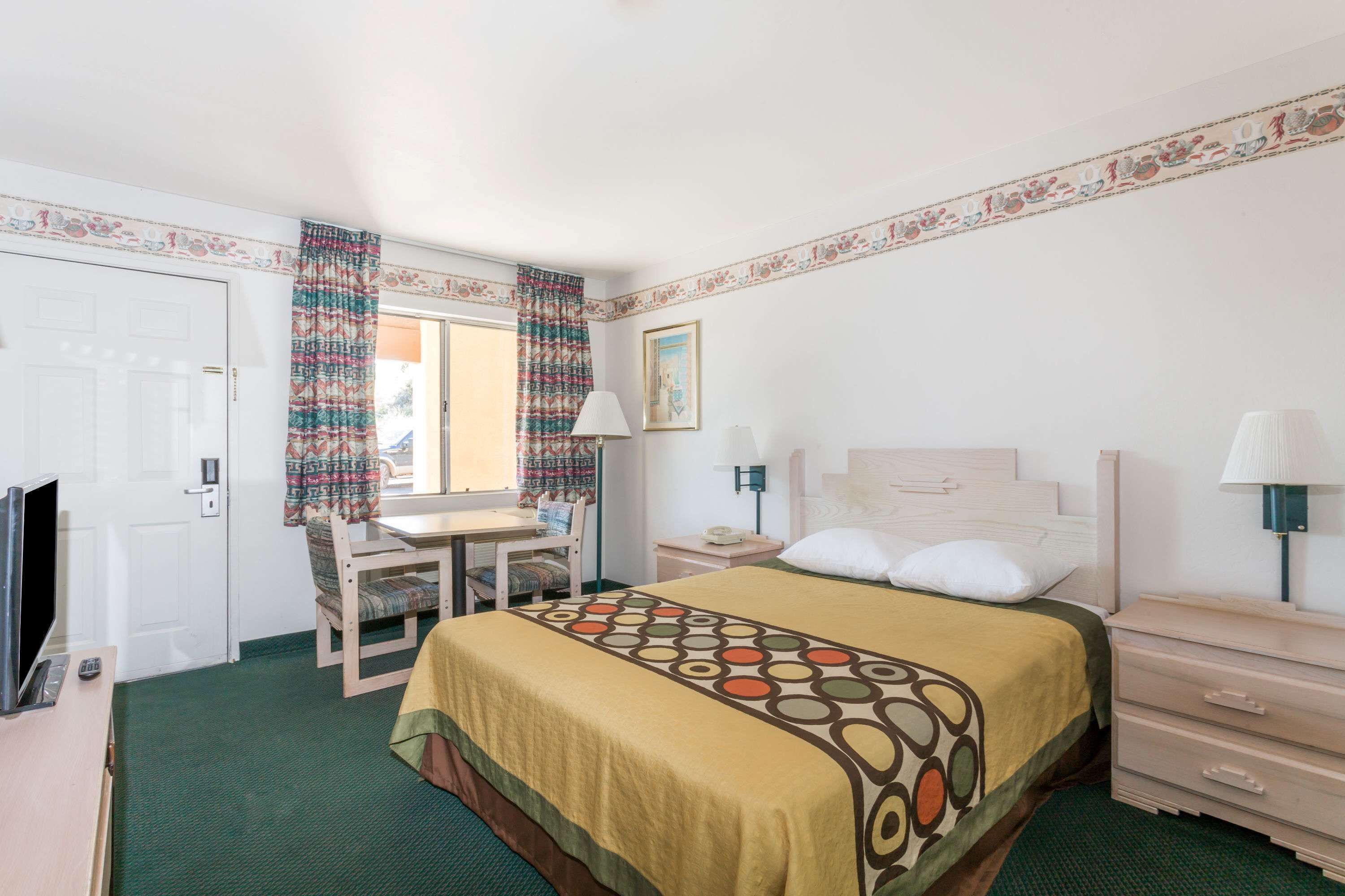 Quarto de hotel com cama, escrivaninha, cadeira, televisão e abajur.