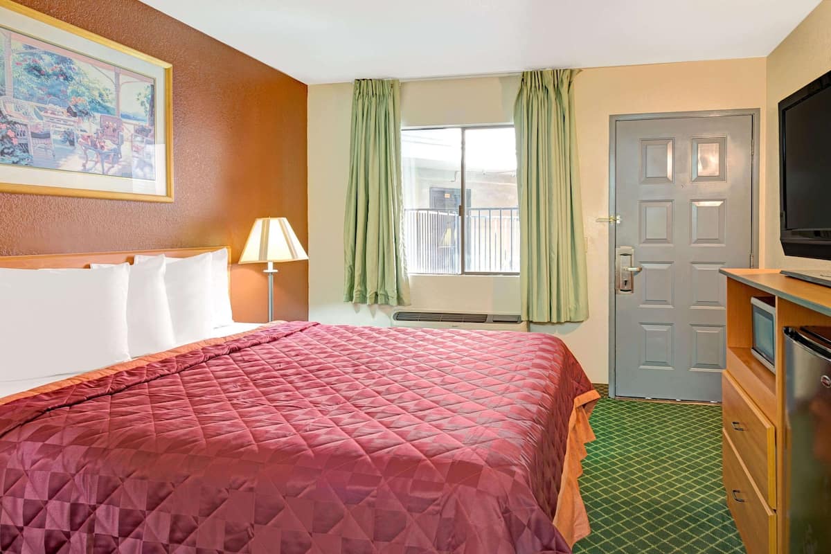 Quarto de hotel com cama, televisão, escrivaninha e janela com cortinas.