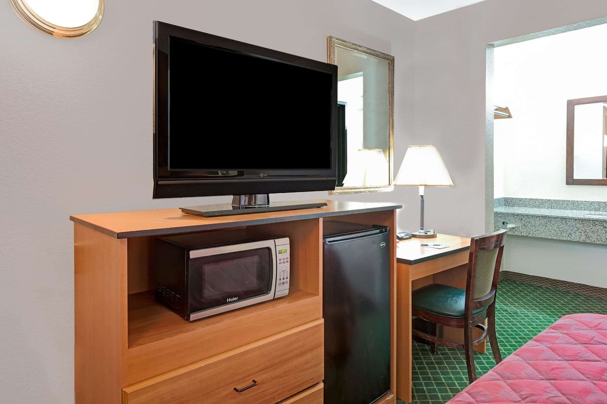 Quarto de hotel com televisão, micro-ondas, frigorífico, secretária, cadeira e cama.