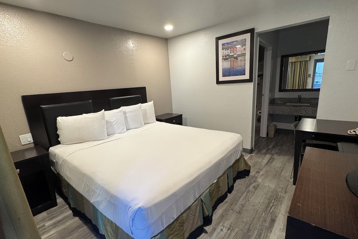 Quarto de hotel com uma cama grande, uma mesa de trabalho e um banheiro visível por uma porta aberta.