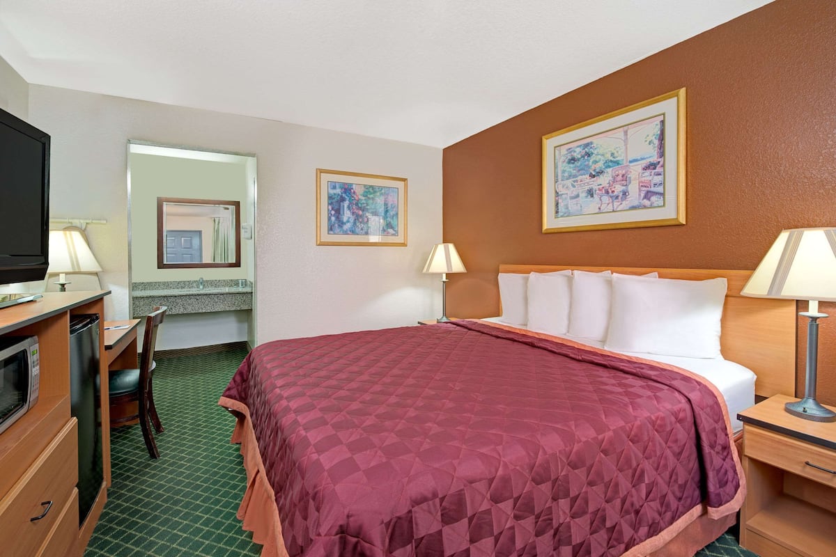 Quarto de hotel com cama, escrivaninha, cadeira, televisão e duas pinturas na parede.