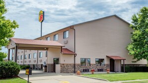 Um motel com área de estacionamento coberta, fachada de tijolos e um grande letreiro.
