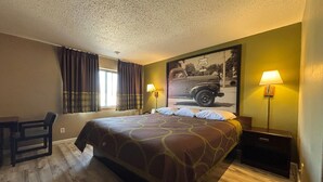 Quarto de hotel com uma cama grande, duas luminárias de cabeceira, uma escrivaninha e janela com cortinas.