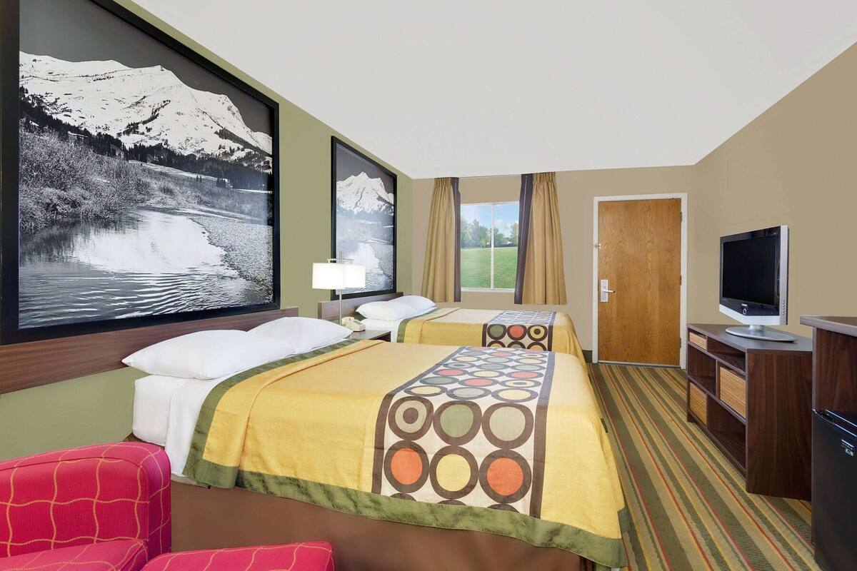 Quarto de hotel com duas camas, televisão, escrivaninha e uma janela grande com cortinas.
